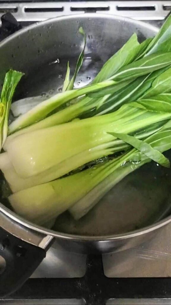 Slices of pak choi blanching in a silver pot of boiling water.