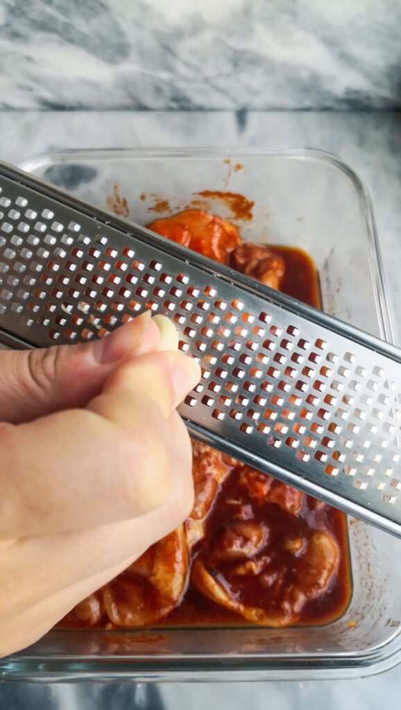 Grating a clove of garlic with a silver microplane into a glass ...